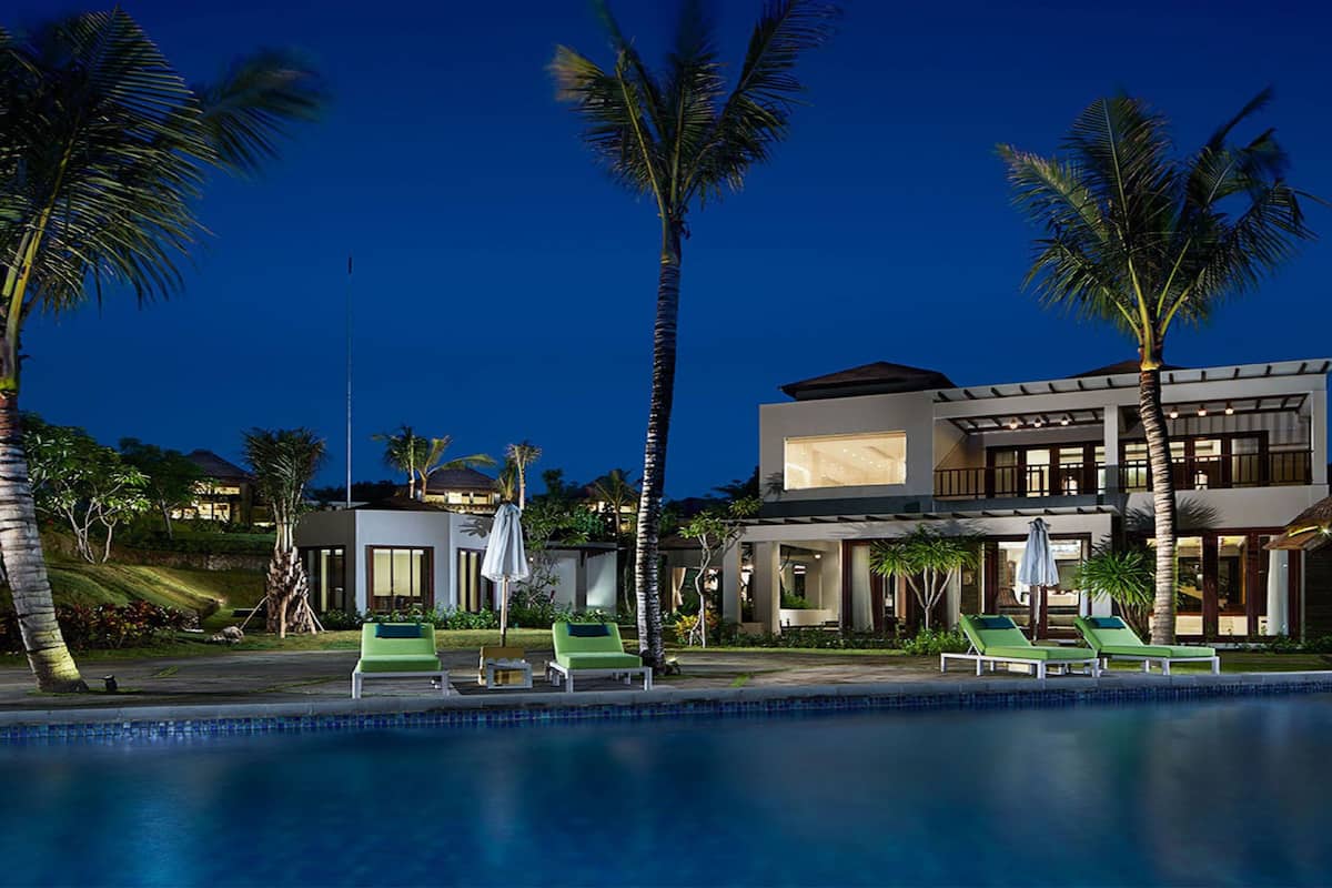 Um resort moderno com piscina, palmeiras e um edifício de dois andares com grandes janelas.