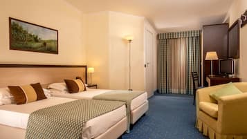 Quarto de hotel com duas camas, uma escrivaninha, uma cadeira, uma televisão e um quadro na parede.