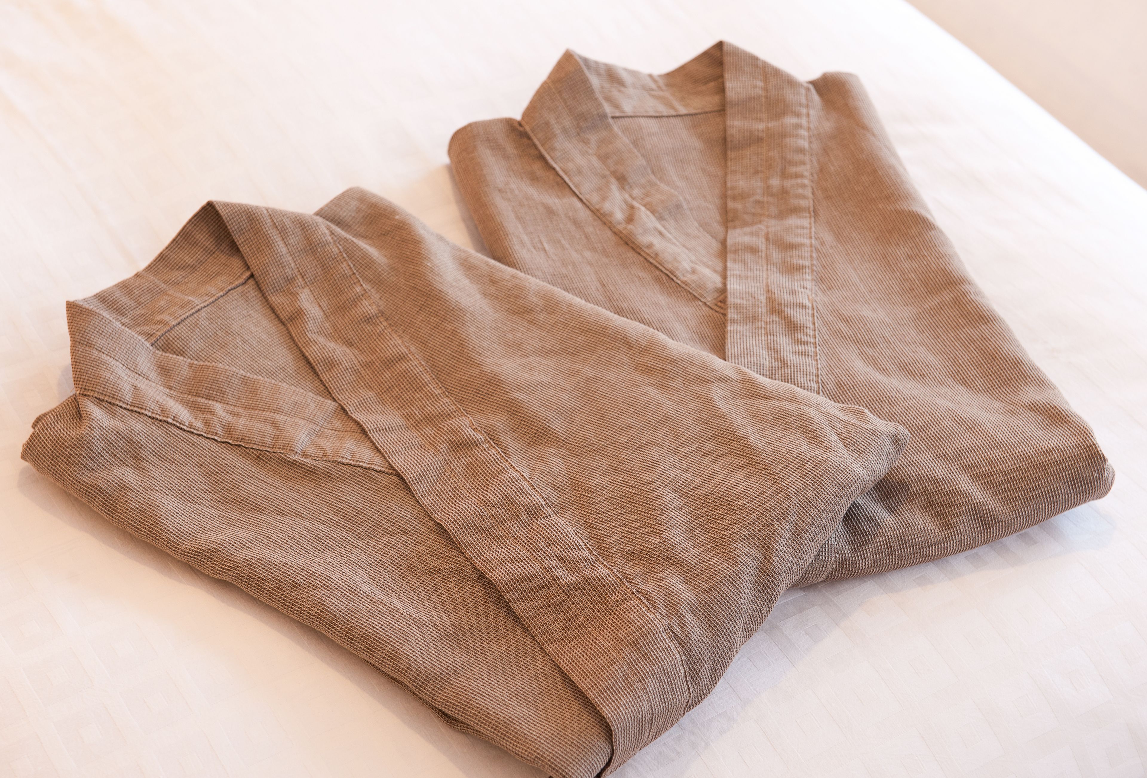 Duas camisas de sarja marrom estendidas sobre uma superfície branca.