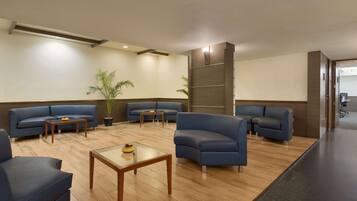 Um lobby moderno com sofás azuis, uma mesa de centro de vidro e piso de madeira.