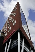 Um hotel alto com design moderno, exibindo uma placa chamativa do 'Mercure Hotel', grandes janelas e um céu claro ao fundo.