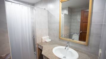 Casa de banho com cortina de chuveiro, pia, espelho e produtos de higiene no balcão.