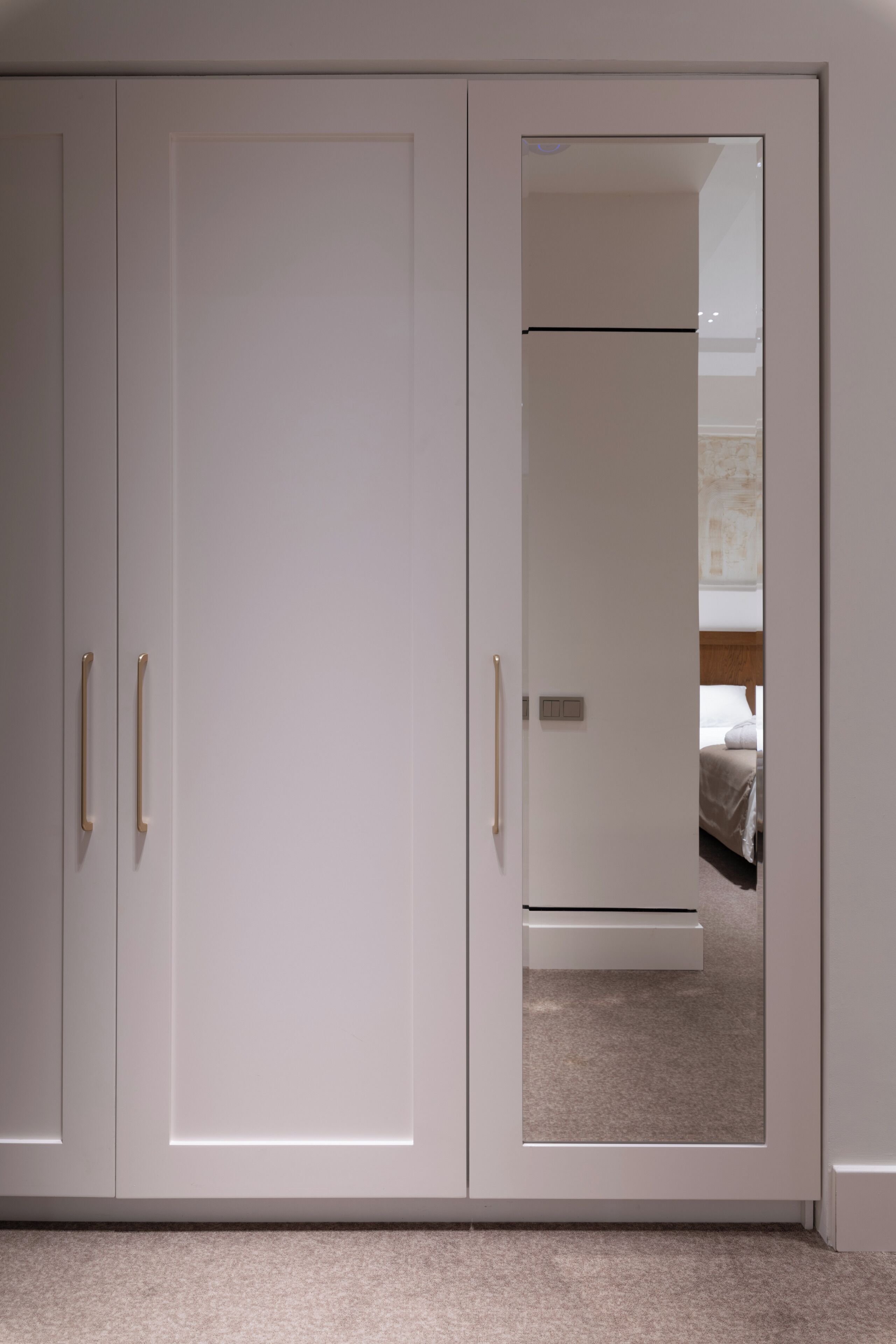 Quarto com um guarda-roupa branco grande e de duas portas, e um espelho.