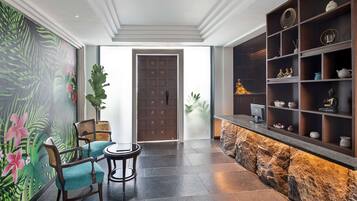 Um lobby moderno com parede de destaque em pedra, balcão de recepção e um mural tropical.