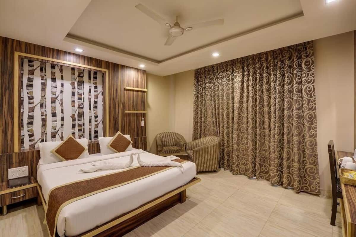 Quarto de hotel com uma cama grande, uma escrivaninha, uma cadeira, um ventilador de teto e cortina estampada.