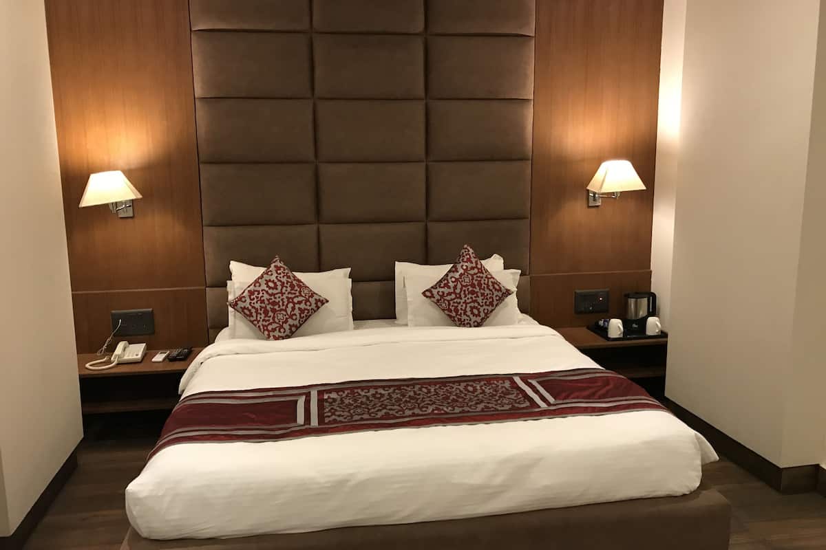 Quarto de hotel com uma cama grande, duas mesas de cabeceira, um telefone, uma cafeteira e duas luminárias na parede.
