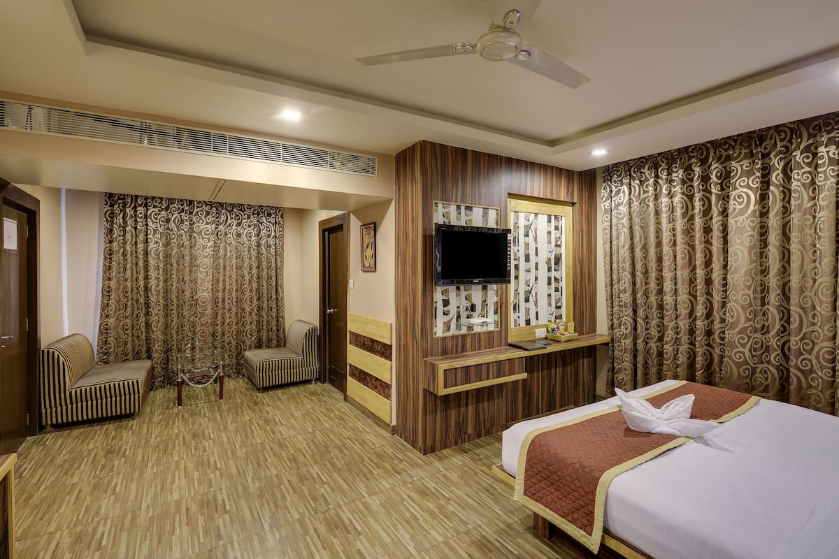 Quarto de hotel com cama, televisão, escrivaninha e duas poltronas.