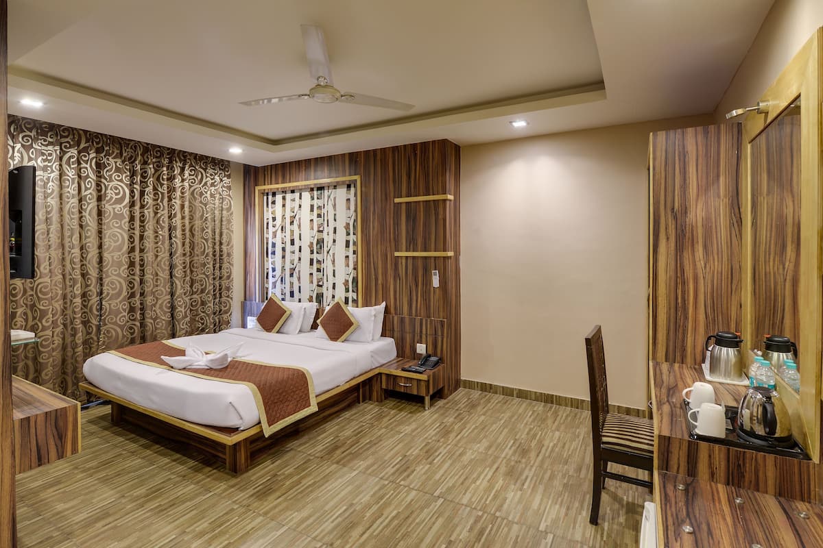 Quarto de hotel com cama, mesa de cabeceira, cadeira e escrivaninha com espelho e cafeteira.