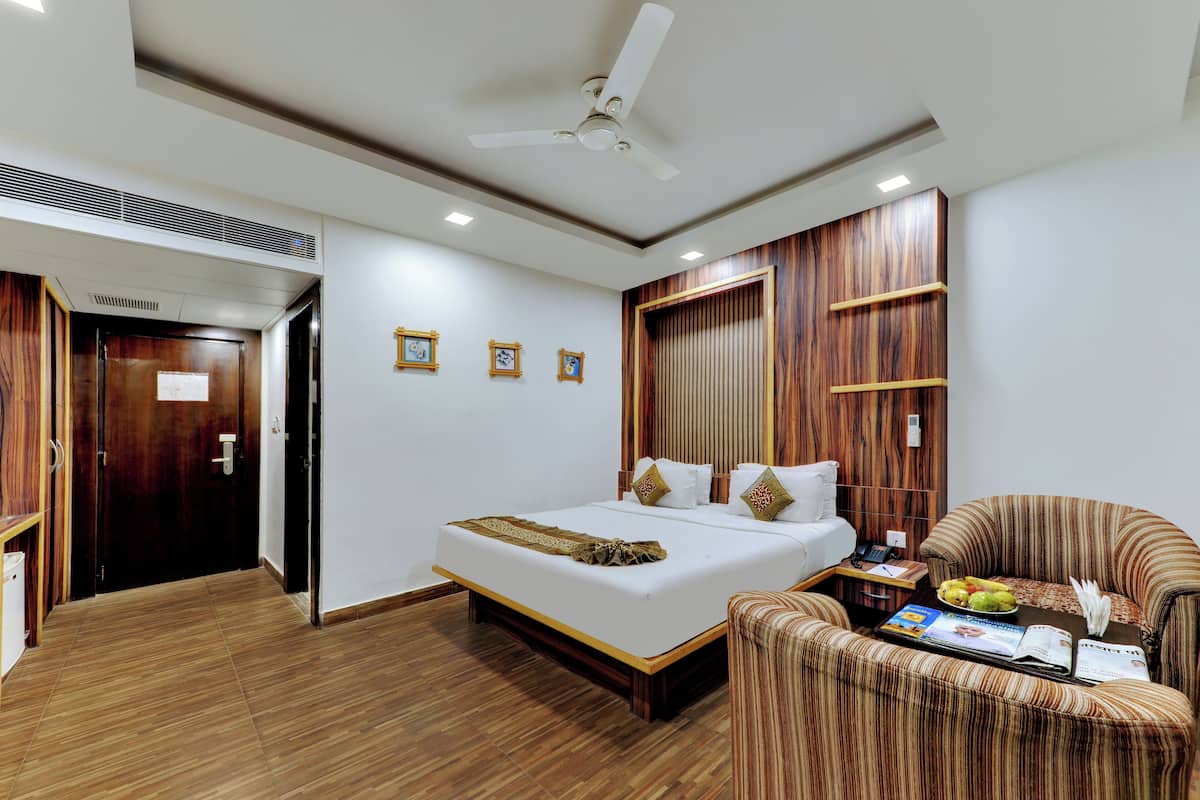 Quarto de hotel com cama, sofá, mesa de jantar e uma revista, e ventilador de teto.