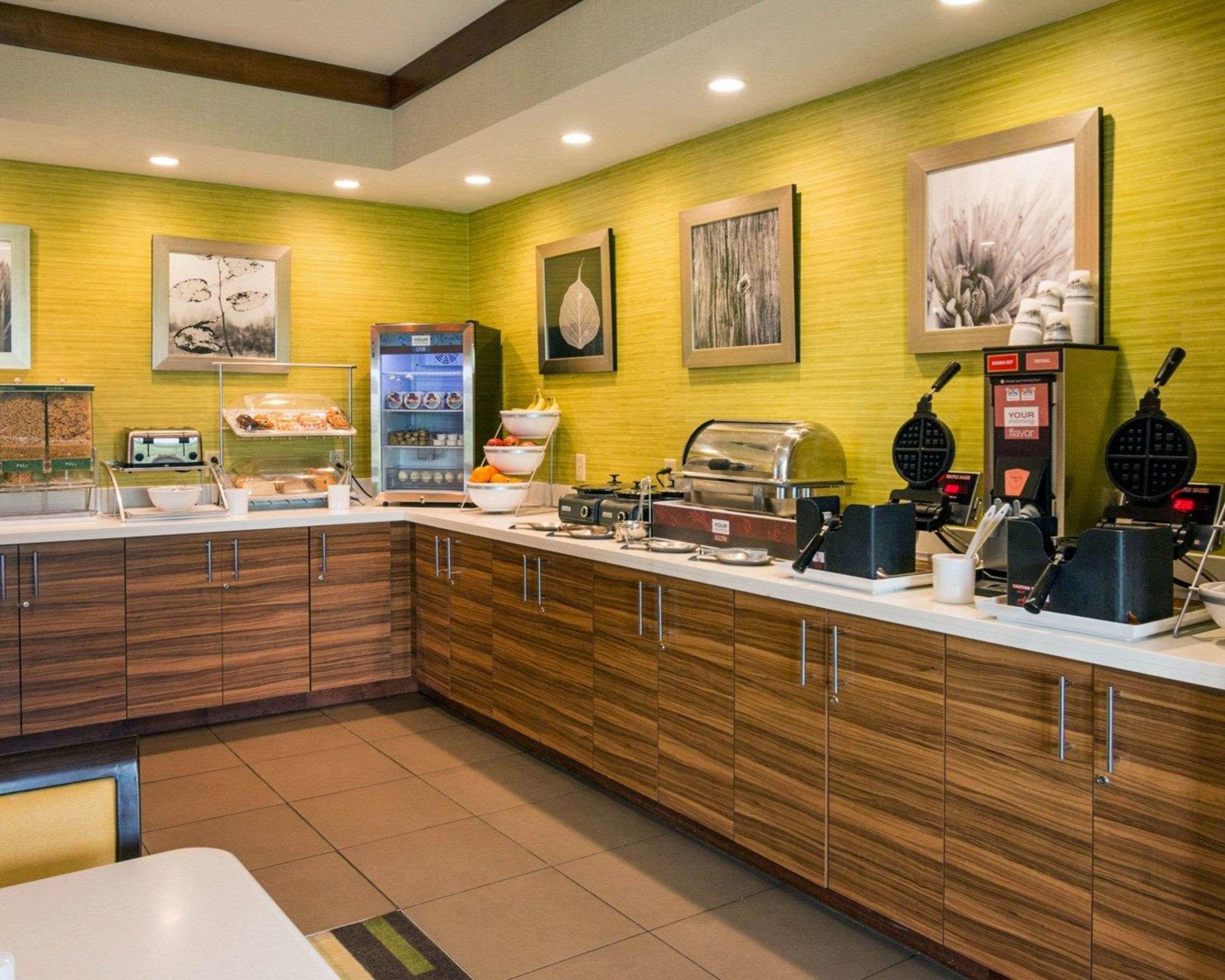 Uma mesa de pequeno-almoço com serviço de buffet, incluindo máquina de café, máquina de waffles e balcão refrigerado.