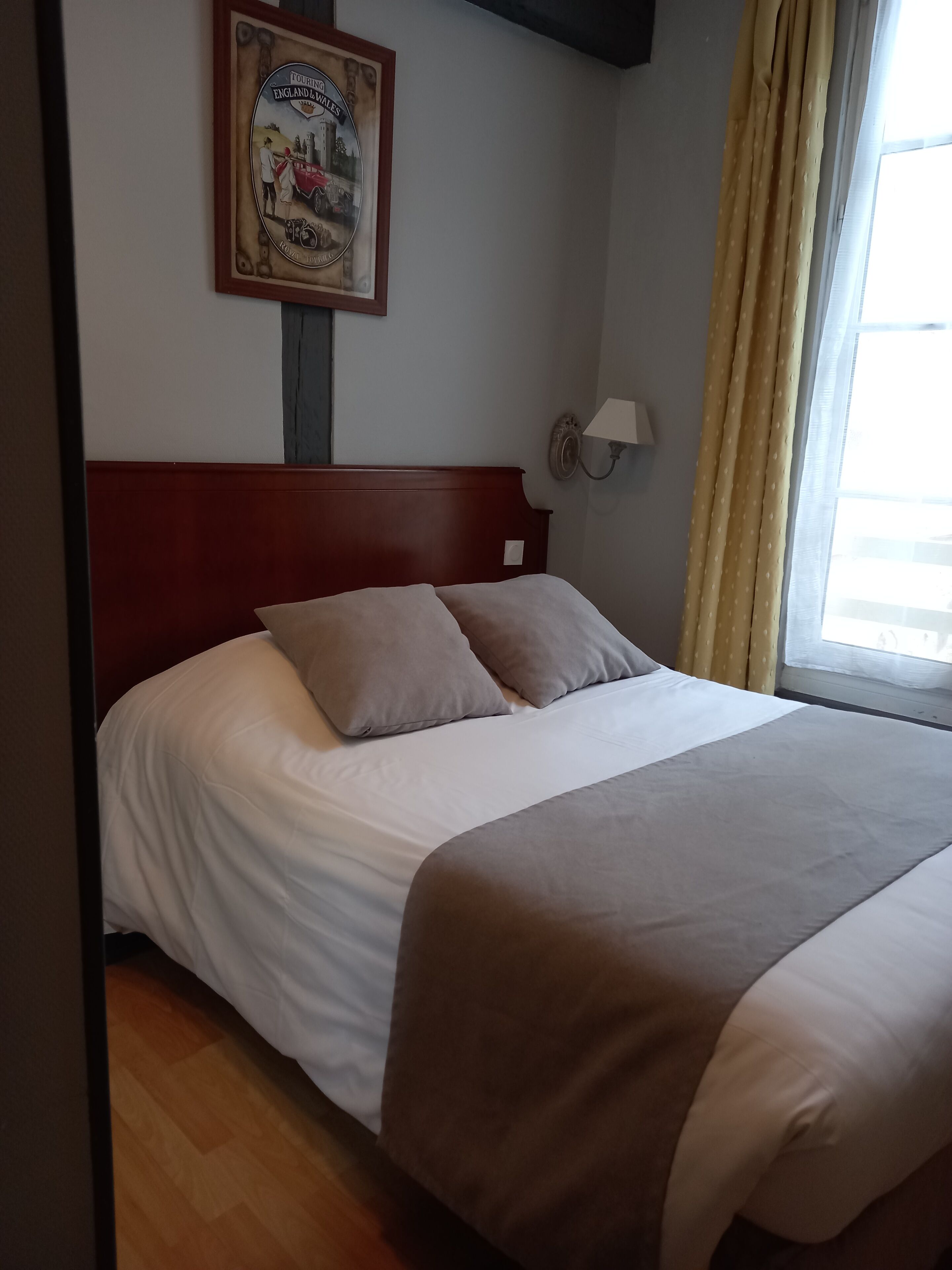Uma cama bem arrumada com cabeceira de madeira, uma luminária na parede e um quadro em cima.