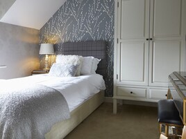 Quarto com cama, mesa de cabeceira, luminária, guarda-roupa e uma cadeira.
