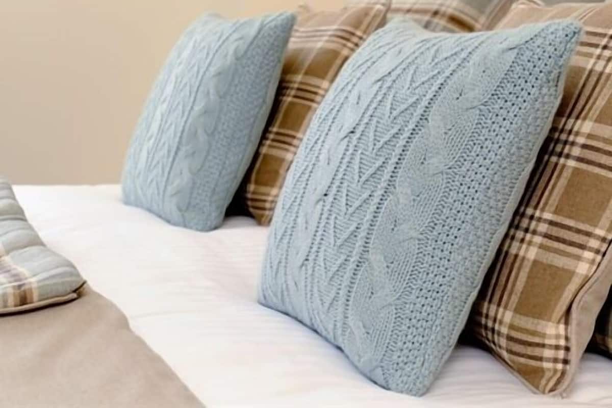 Uma cama com almofadas de tricô e xadrez.