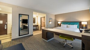 Quarto de hotel com cama, escrivaninha, cadeira e espelho.