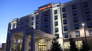 Um hotel Hampton Inn com fachada moderna, entrada coberta e céu claro.
