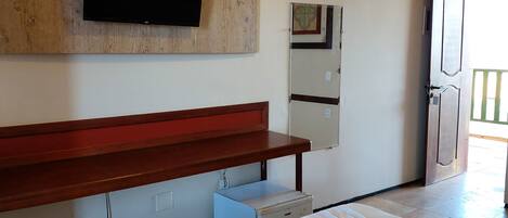 Quarto de hotel com cama, televisão fixada na parede, espelho e porta que dá para uma varanda.