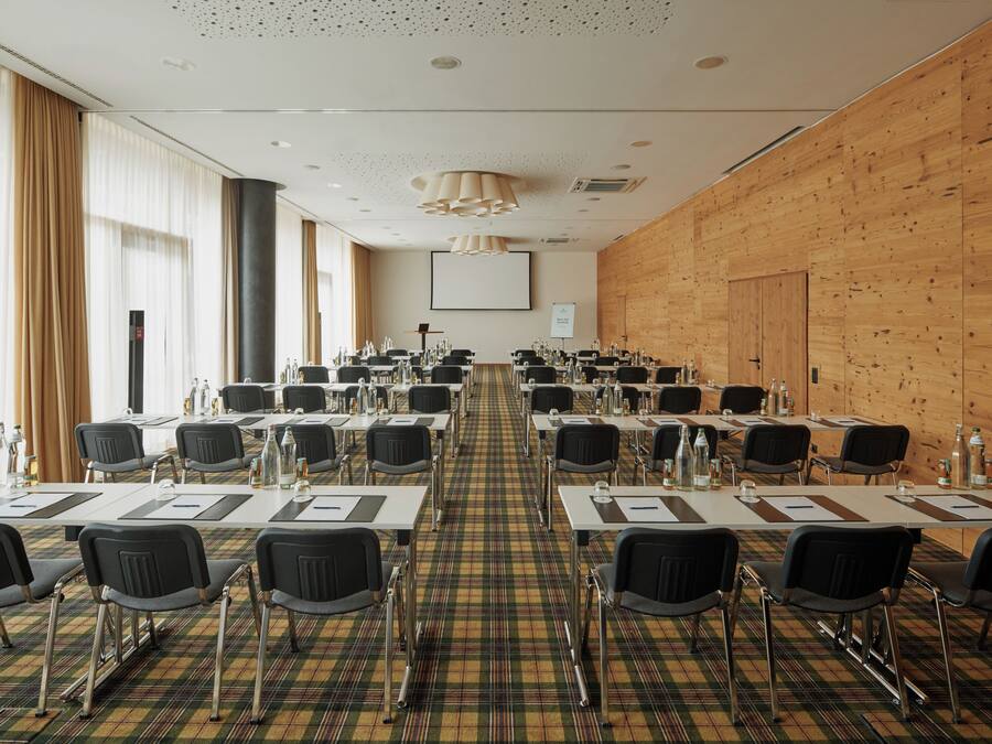 Uma sala de conferências com uma mesa comprida, cadeiras, uma tela de projetor e uma parede de madeira.