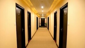 Corredor de hotel com portas em ambos os lados, piso coberto de carpete e iluminação no teto.