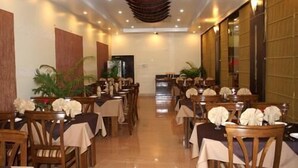 Uma sala de jantar de hotel com várias mesas, cadeiras e plantas em vasos.