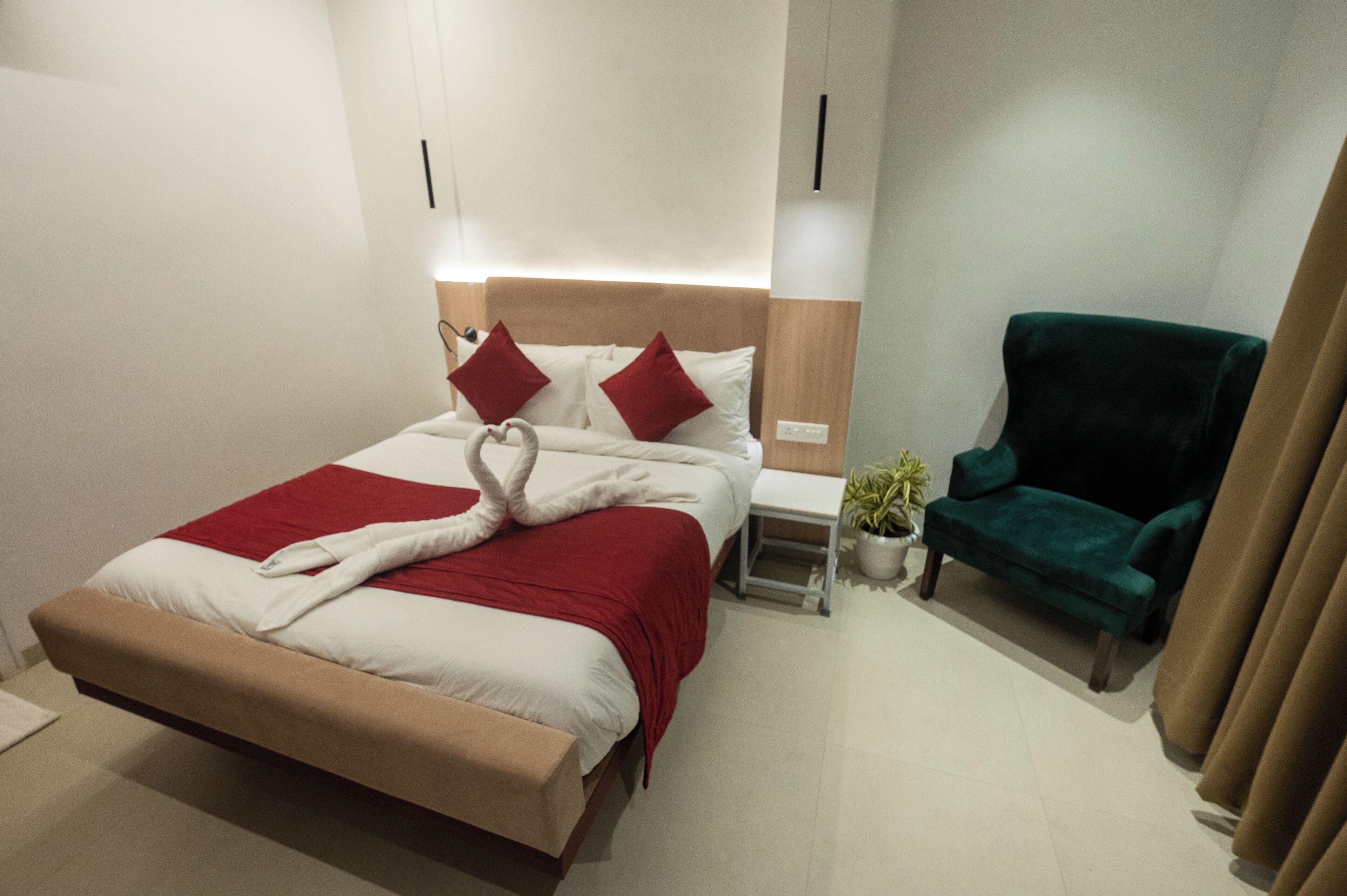 Quarto de hotel moderno com uma cama bem arrumada, uma poltrona verde e uma pequena planta em vaso.