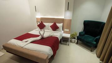 Quarto de hotel moderno com uma cama bem arrumada, uma poltrona verde e uma pequena planta em vaso.