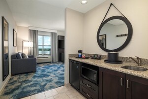 Quarto de hotel com área de estar, cozinha compacta e um espelho grande.