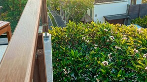 Um deck de madeira com vista para uma área ajardinada com plantas tropicais e edifícios com telhados piramidais.