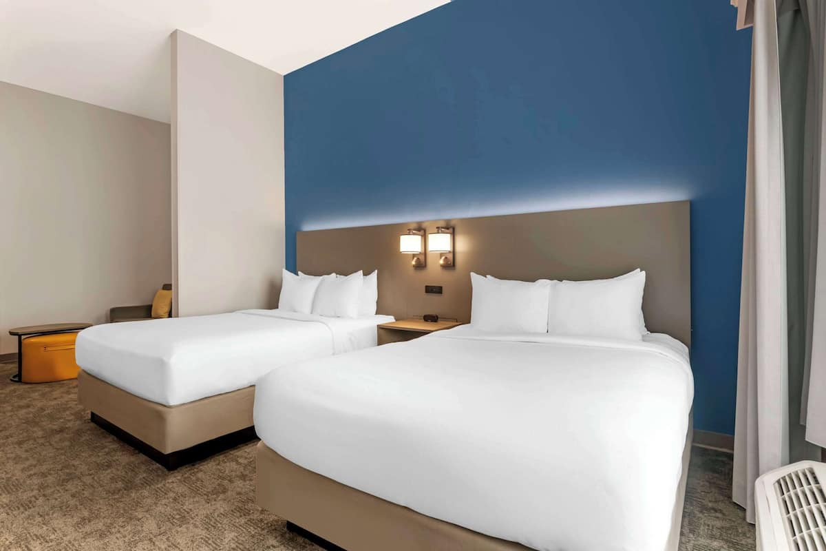 Quarto de hotel com duas camas, uma mesa de cabeceira e uma escrivaninha.
