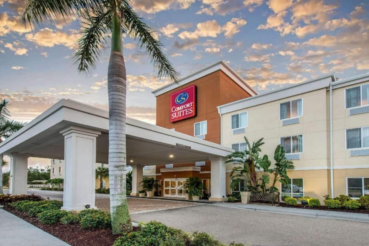 Um hotel Comfort Suites com entrada coberta, palmeiras e céu claro.