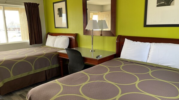 Quarto de hotel com duas camas, uma escrivaninha, uma cadeira, um abajur e um espelho.