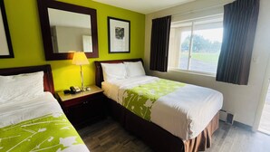 Quarto de hotel com duas camas, uma mesa de cabeceira com abajur, uma janela com cortinas e um espelho na parede.