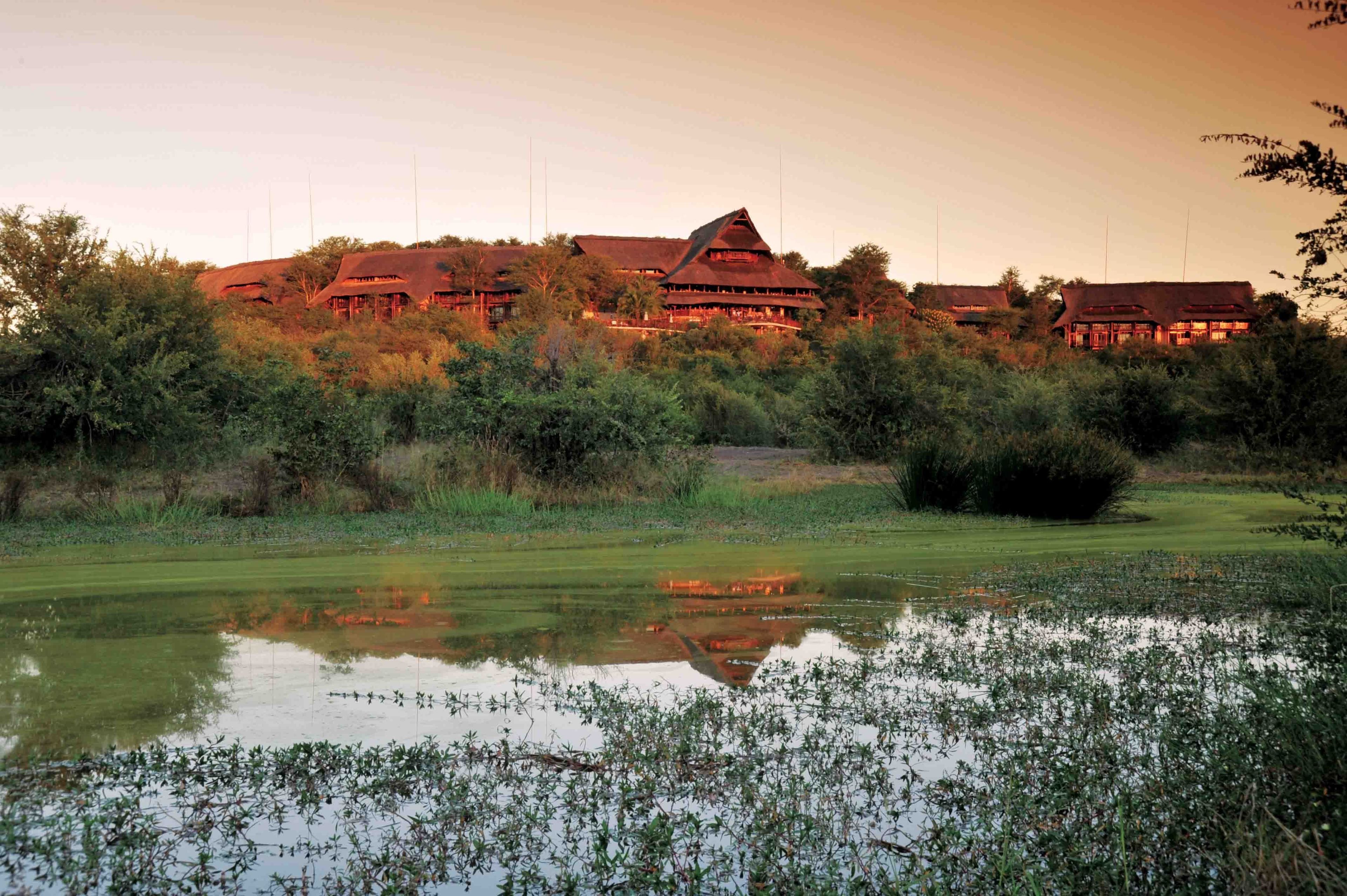 Resort com vários edifícios, um grande corpo d'água em primeiro plano e vegetação ao redor.