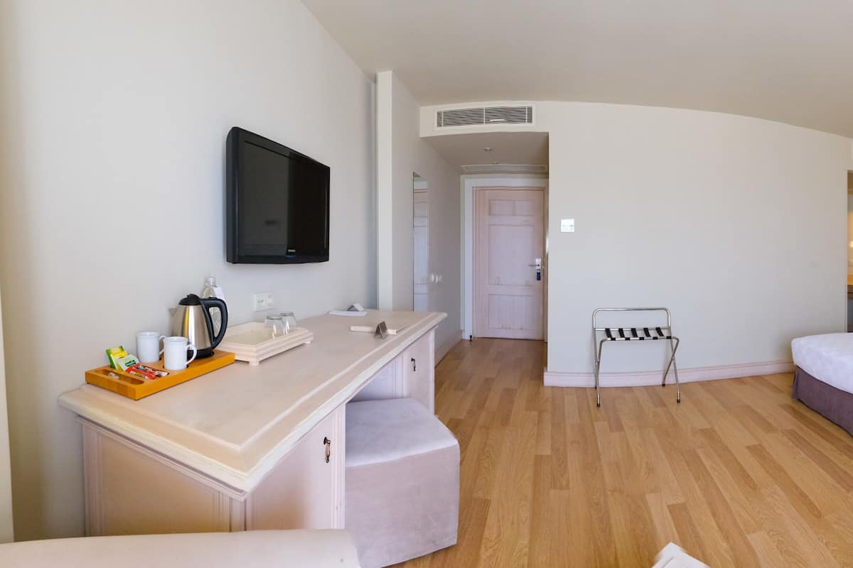 Quarto de hotel com escrivaninha, duas camas, televisão e uma pequena cozinha.