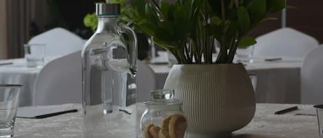 Uma mesa com uma garrafa de vidro, um pote de biscoitos e um vaso de planta.