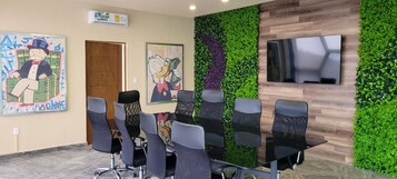 Uma sala de conferências com parede verde, parede de destaque em madeira e uma TV de tela plana.