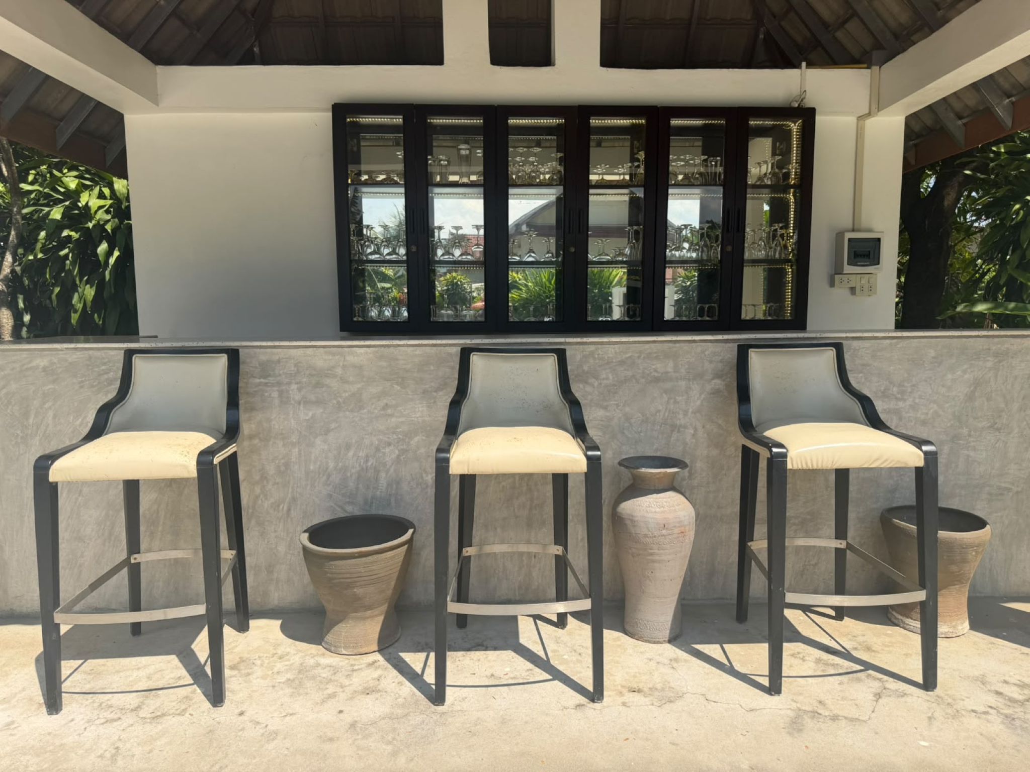 Uma área de estar com três banquetas e um vaso grande em frente a uma parede com uma janela.