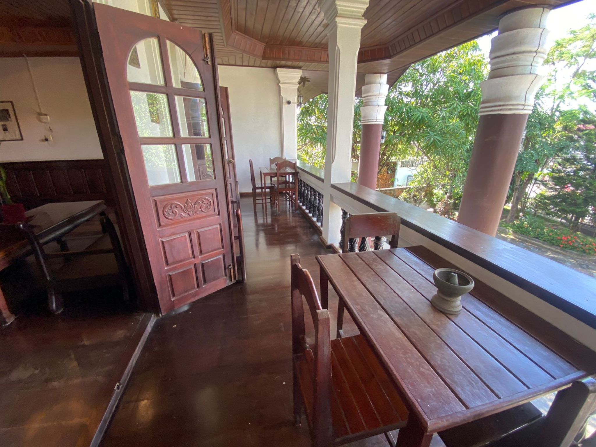 Interior em madeira com uma grande porta aberta, bancos de madeira e vista para o verde lá fora.