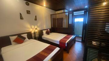 Quarto de hotel com duas camas, uma mesa de cabeceira com abajur, cabeceira de madeira e vista para o exterior.