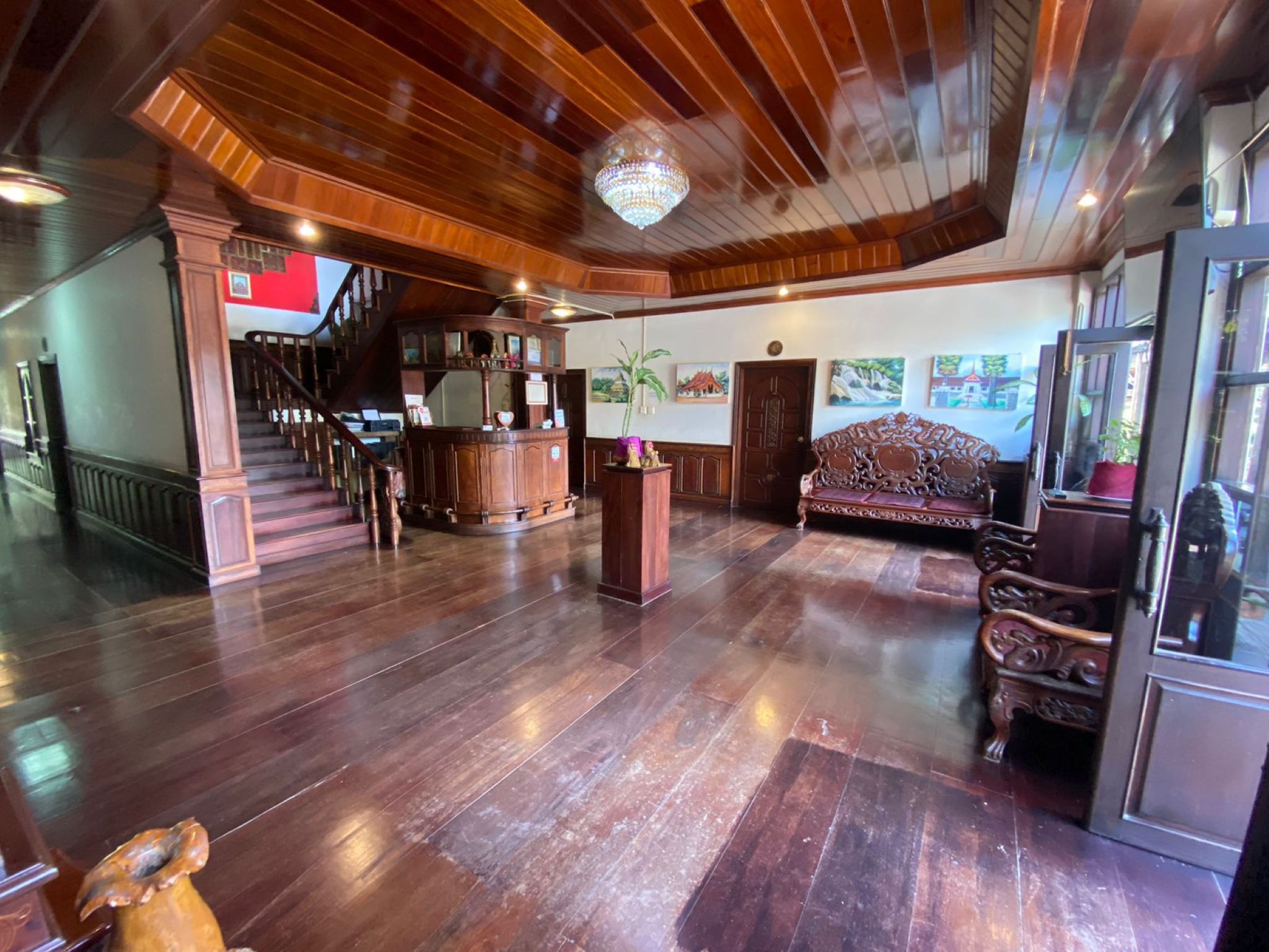 Um hall amplo com escada de madeira, balcão de recepção e um sofá.