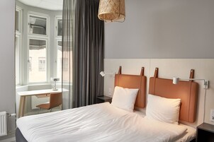 Quarto de hotel bem organizado, com uma cama grande, uma mesa de trabalho e uma janela com cortinas.