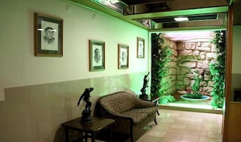 Uma área de recepção com retratos emoldurados na parede, uma estátua sobre uma mesa e uma parede de pedra com plantas.