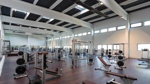 Uma academia espaçosa com diversos equipamentos de exercício, amplas janelas e teto alto.