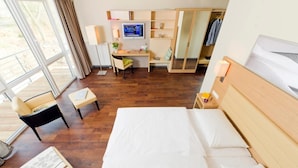 Quarto de hotel com cama, escrivaninha, cadeira, televisão e guarda-roupa.
