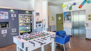 Espaço moderno em ambientes internos com mesa de pebolim, máquina de vendas automática e uma cadeira azul.