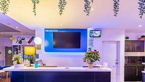 Uma receção com um ecrã de televisão, um sinal azul a dizer 'RECEÇÃO' e uma planta em vaso.
