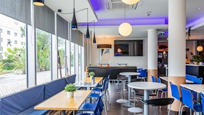Um espaço interior moderno com mesas, cadeiras, área de bar e grandes janelas com vista para o exterior.
