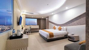 Quarto de hotel moderno com uma cama grande, uma escrivaninha, uma cadeira e vista para a paisagem urbana através de uma janela ampla.