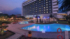 Um hotel com uma piscina grande, área coberta e fachada bem iluminada.