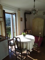 Uma sala de jantar com uma mesa redonda, cadeiras, um vaso de planta e vista para o exterior.