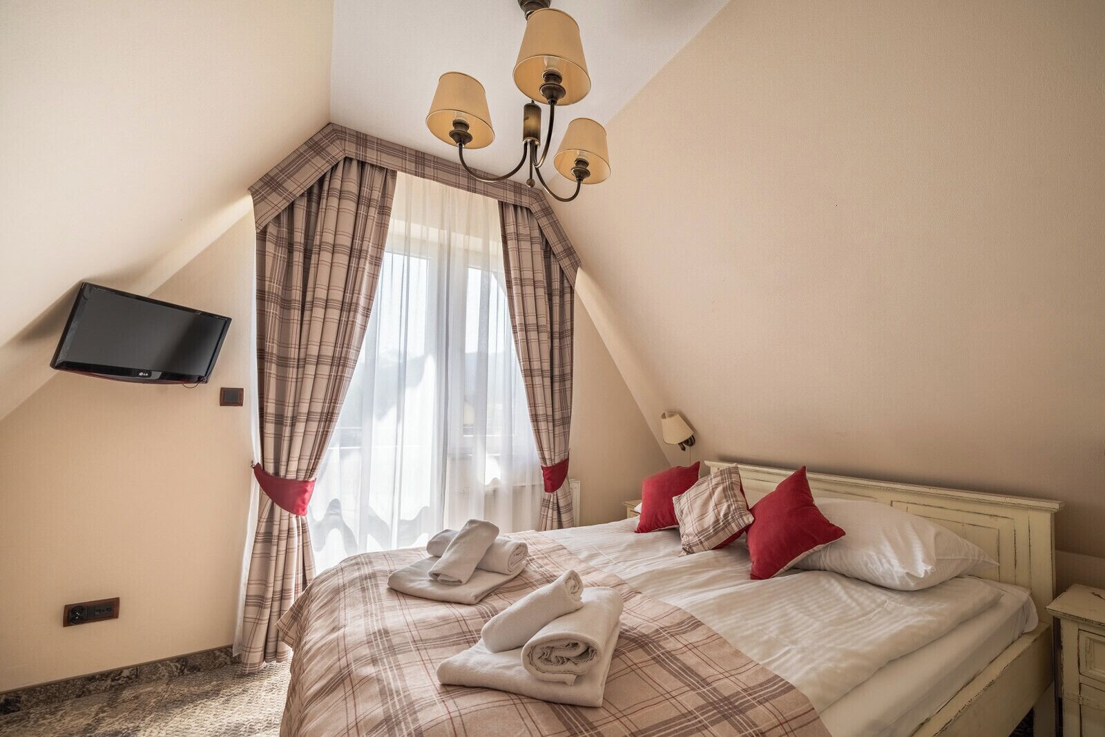 Quarto com cama, almofadas, televisão de tela plana na parede e um candelabro.